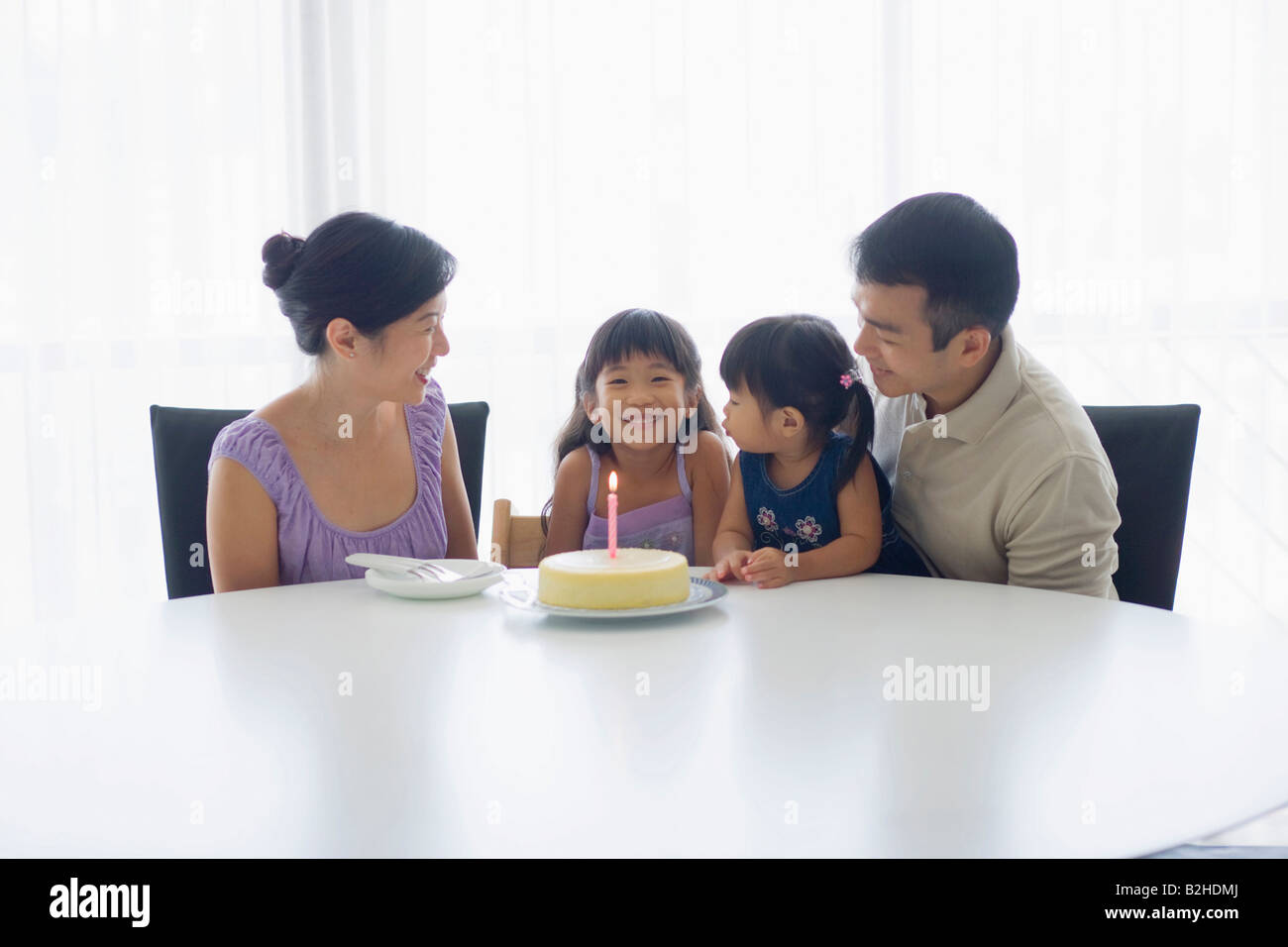 Mid adult couple sitting in front of a birthday cake with their two ...