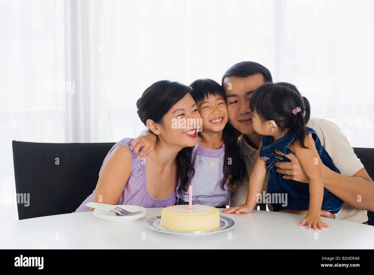 Mid adult couple sitting in front of a birthday cake with their two ...