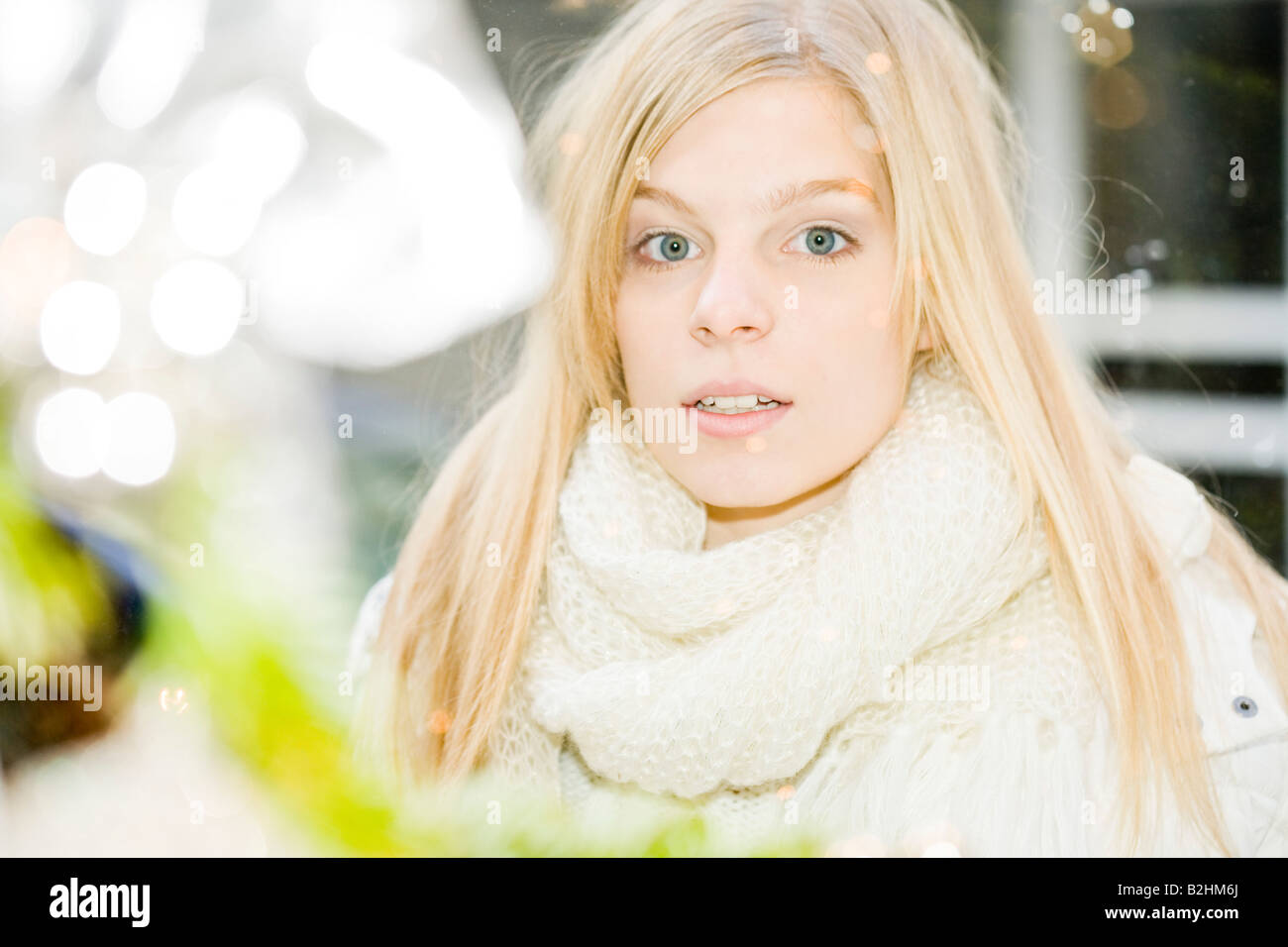 portrait of young woman looking through shop window with christmas ...