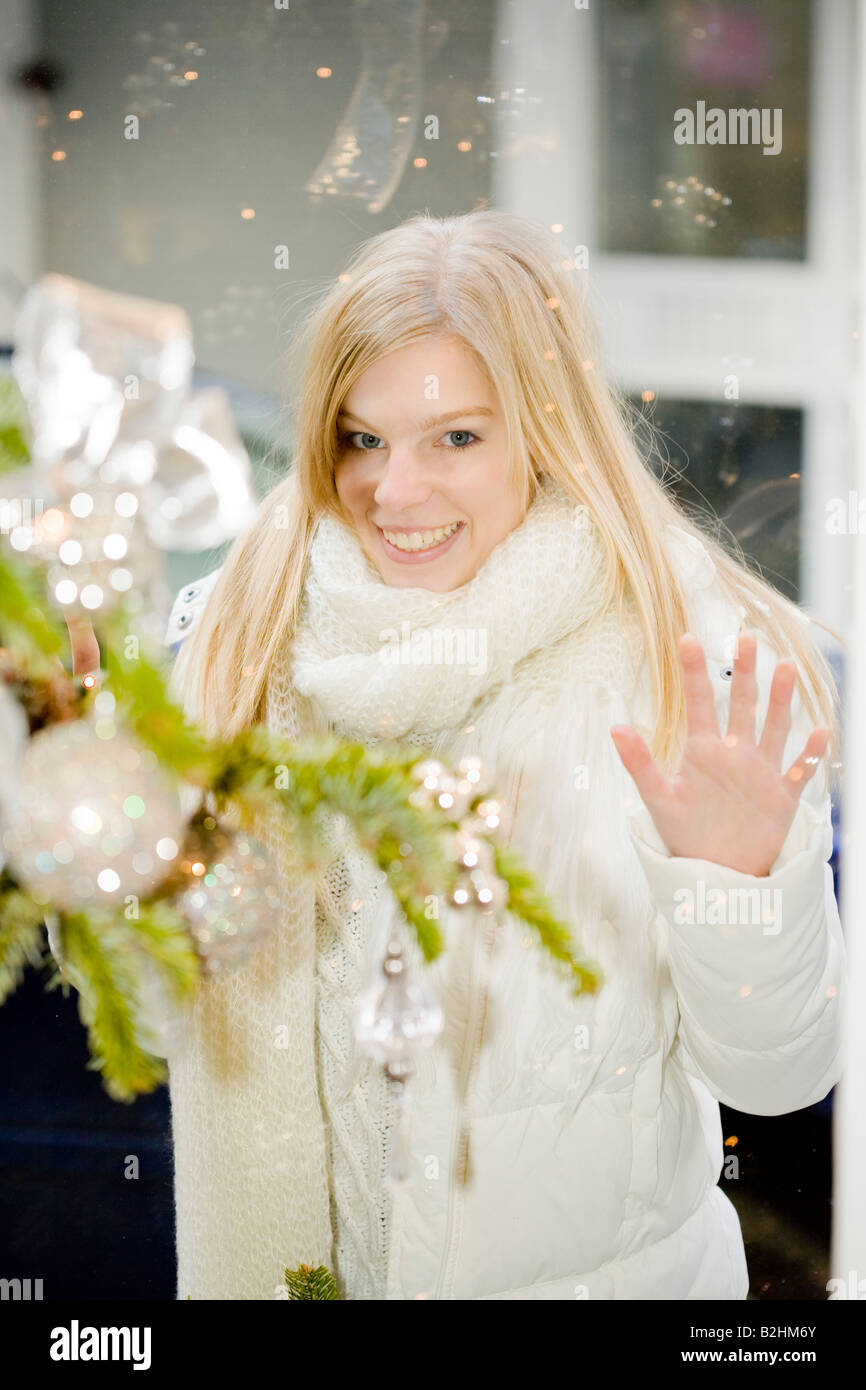 portrait of young woman looking through shop window with christmas ...
