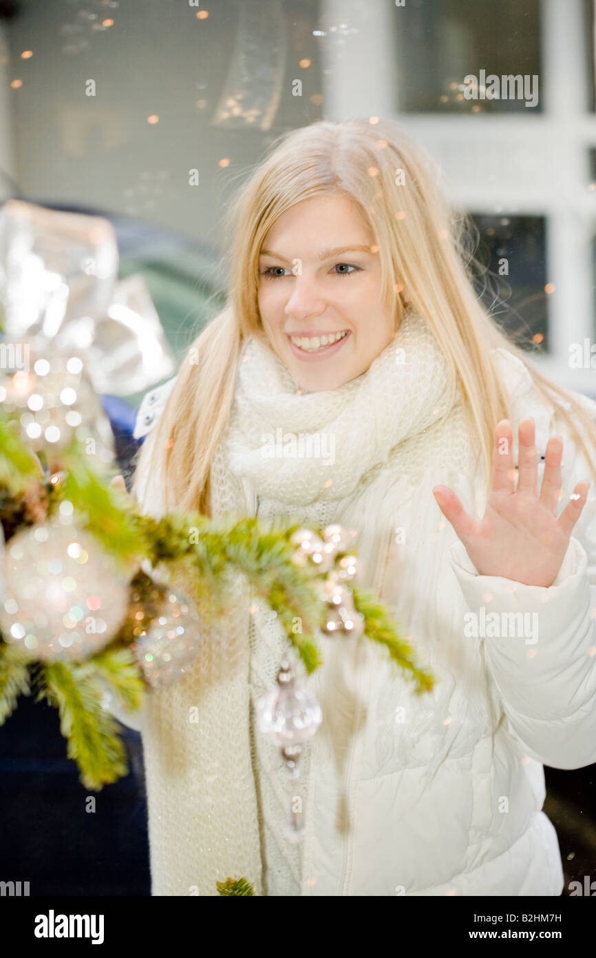 portrait of young woman looking through shop window with christmas ...