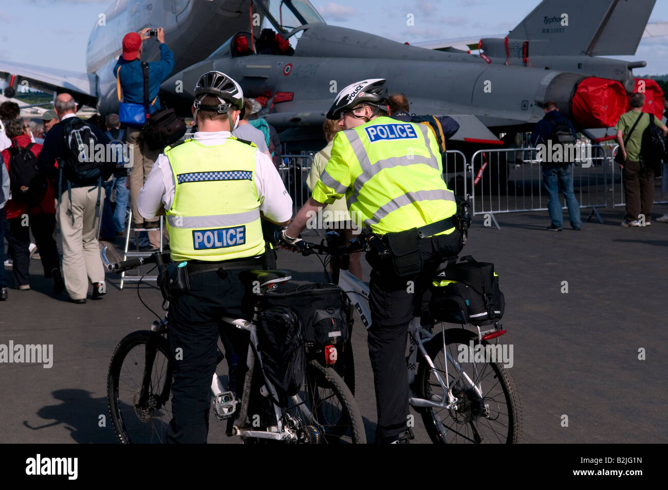 Two 2 police men on bycycles in yellow jackets sitting talking at a ...
