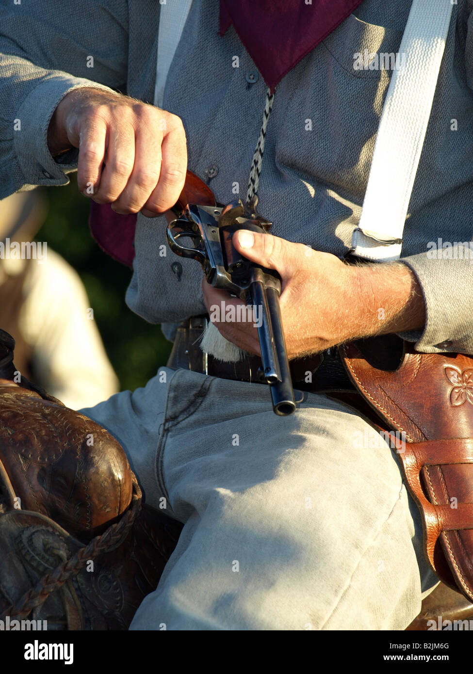 A cowboy loading bullets into his gun while in the saddle on horseback ...