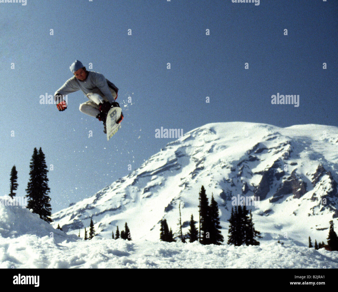 Snowboarder flies off snow drift on snowboard at Mt. Rainier Washington ...