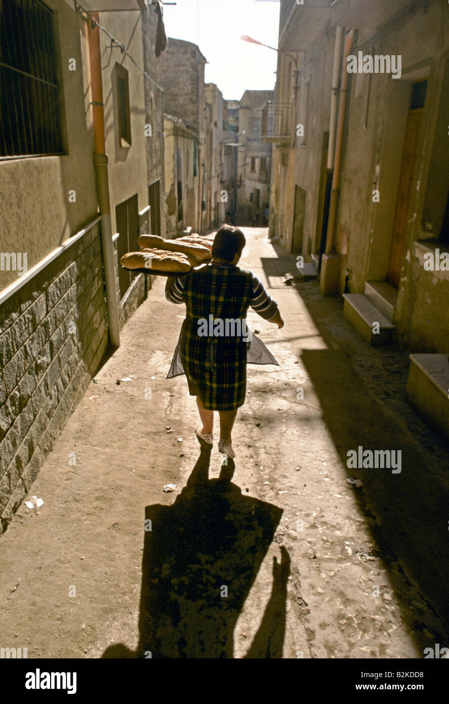 italian woman carrying a tray of fresh bread loaves down a sunny ...