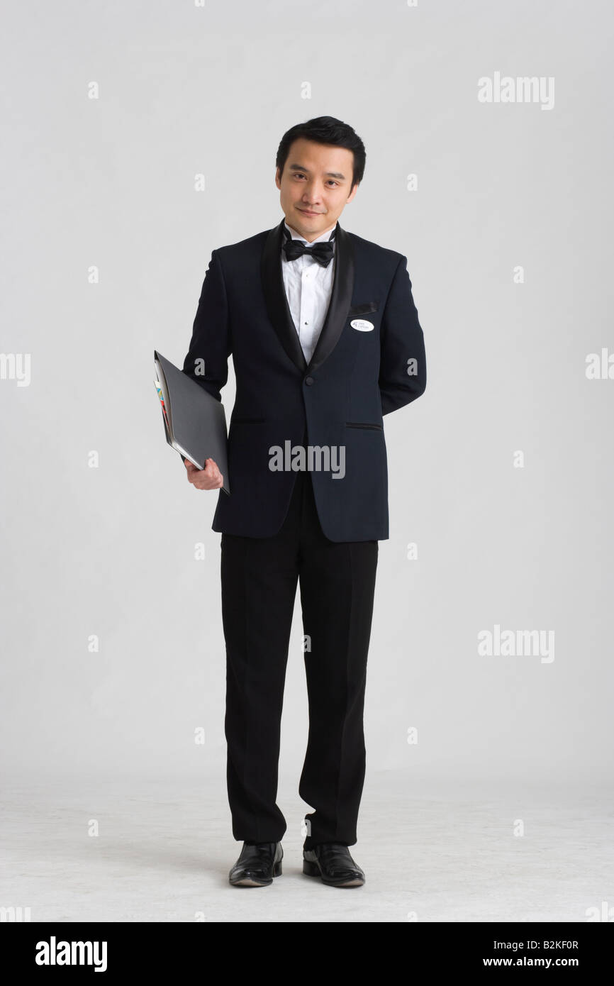 Portrait of a waiter holding a menu and standing with hands behind back ...