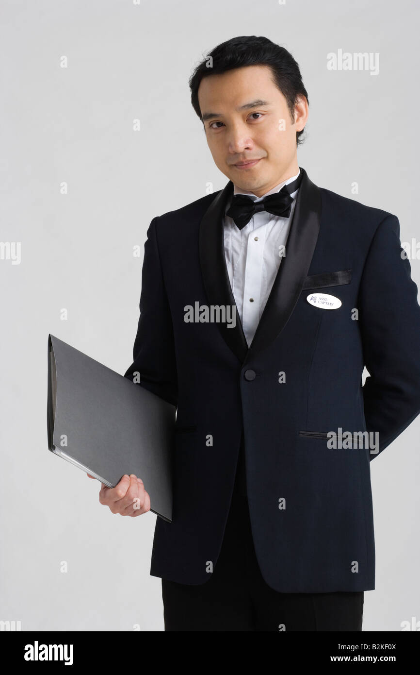 Portrait of a waiter holding a menu and standing with hands behind back ...
