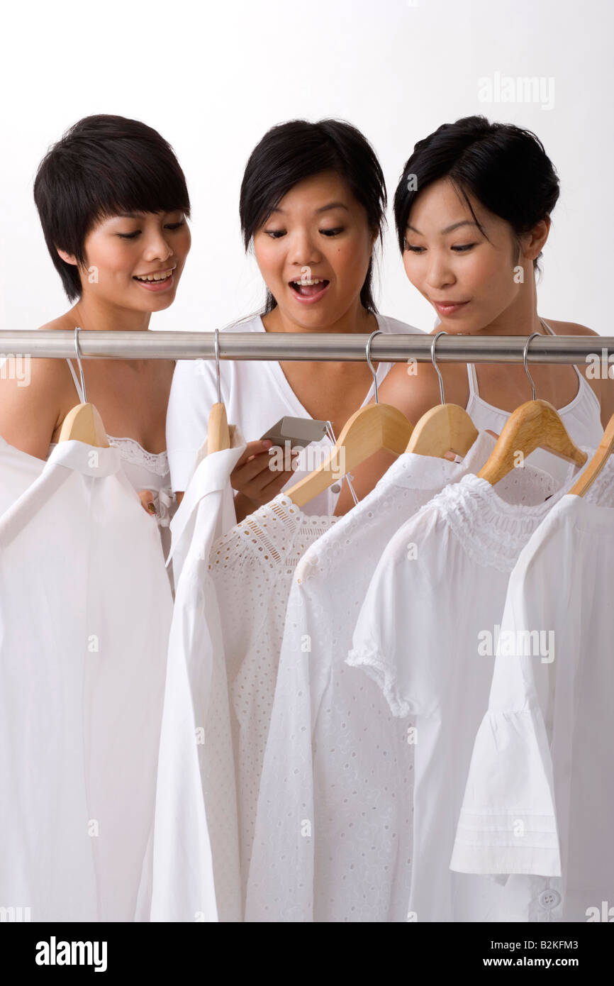 Three young women looking at the price tag of a dress in a clothing ...