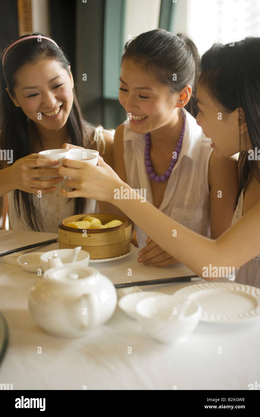 Three young women toasting with tea cups in a restaurant and smiling ...