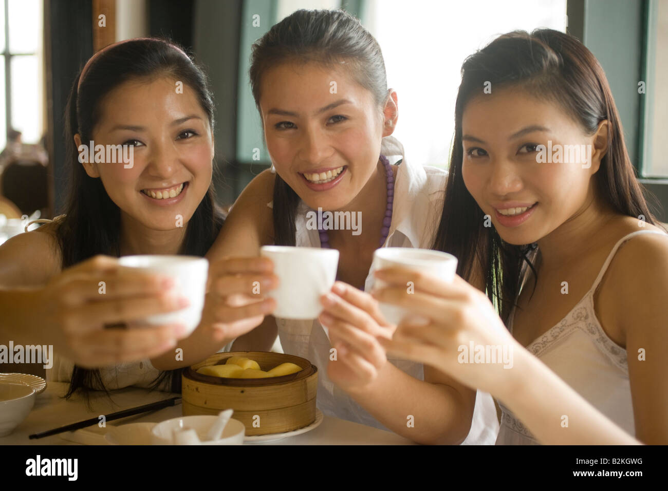 Portrait of three young women having tea in a restaurant and smiling ...