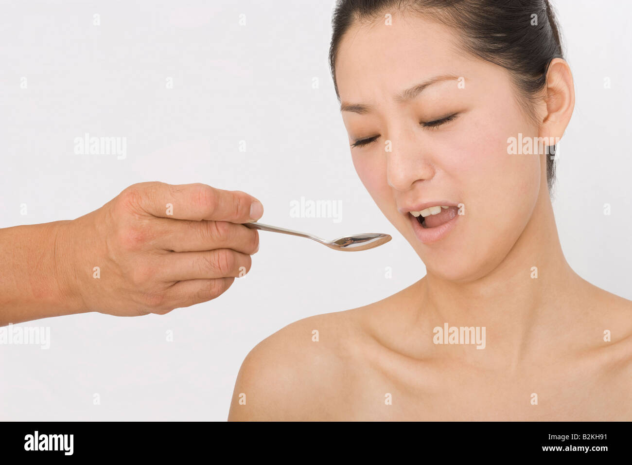Close-up of a person's hand giving a spoon of medicine to a young woman ...