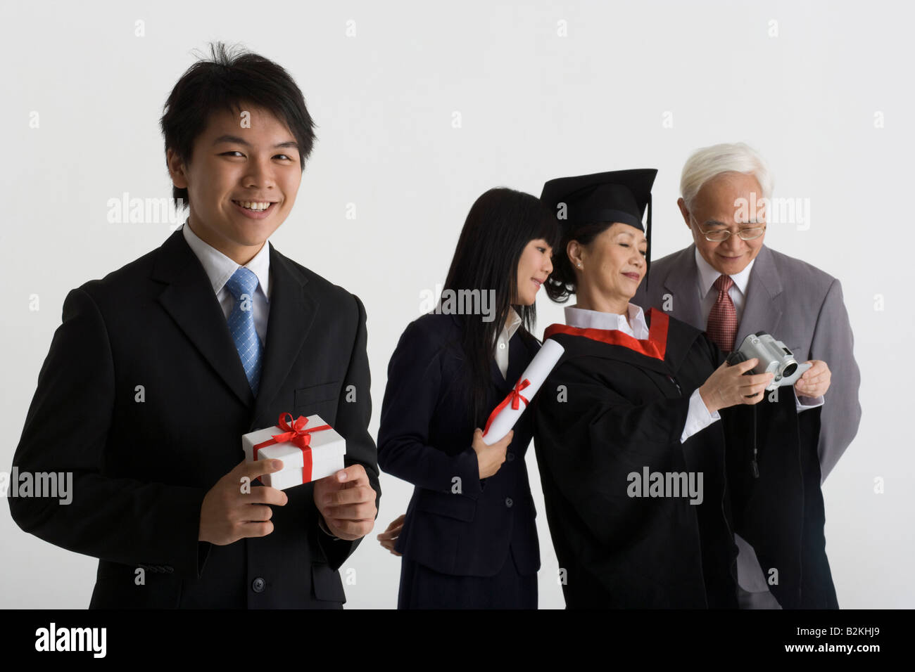Young man holding a gift with his family looking at a home video camera ...