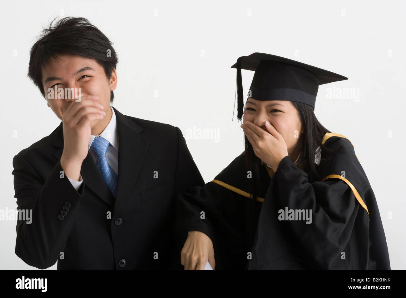 Young man and a young female graduate laughing with covering their ...
