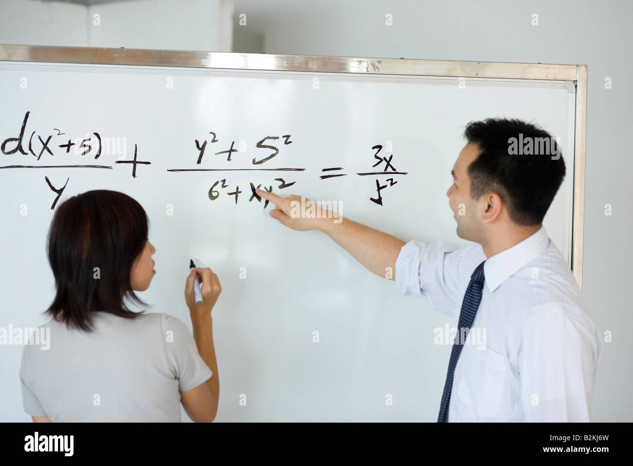 Professor pointing at a whiteboard with his student standing beside him ...