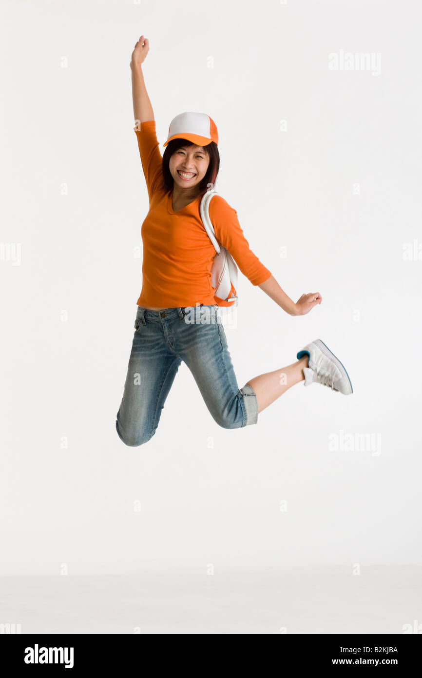 Portrait of a young woman jumping with her hand raised and smiling ...