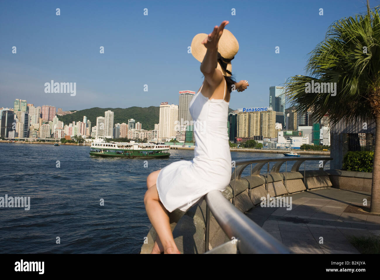 Side profile of a young woman sitting on a railing with arms ...