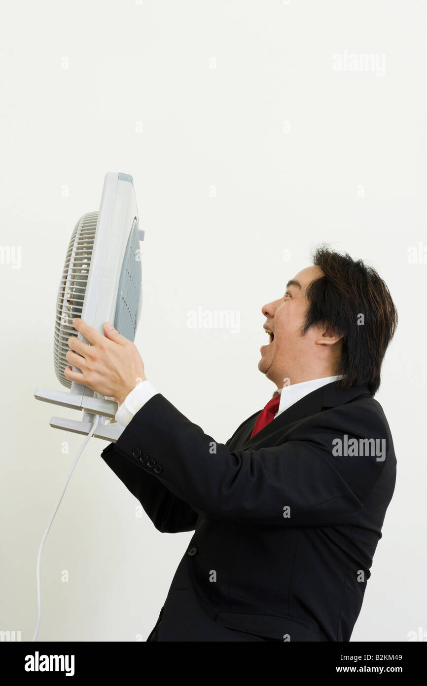 Side profile of a businessman holding an electric fan and laughing ...