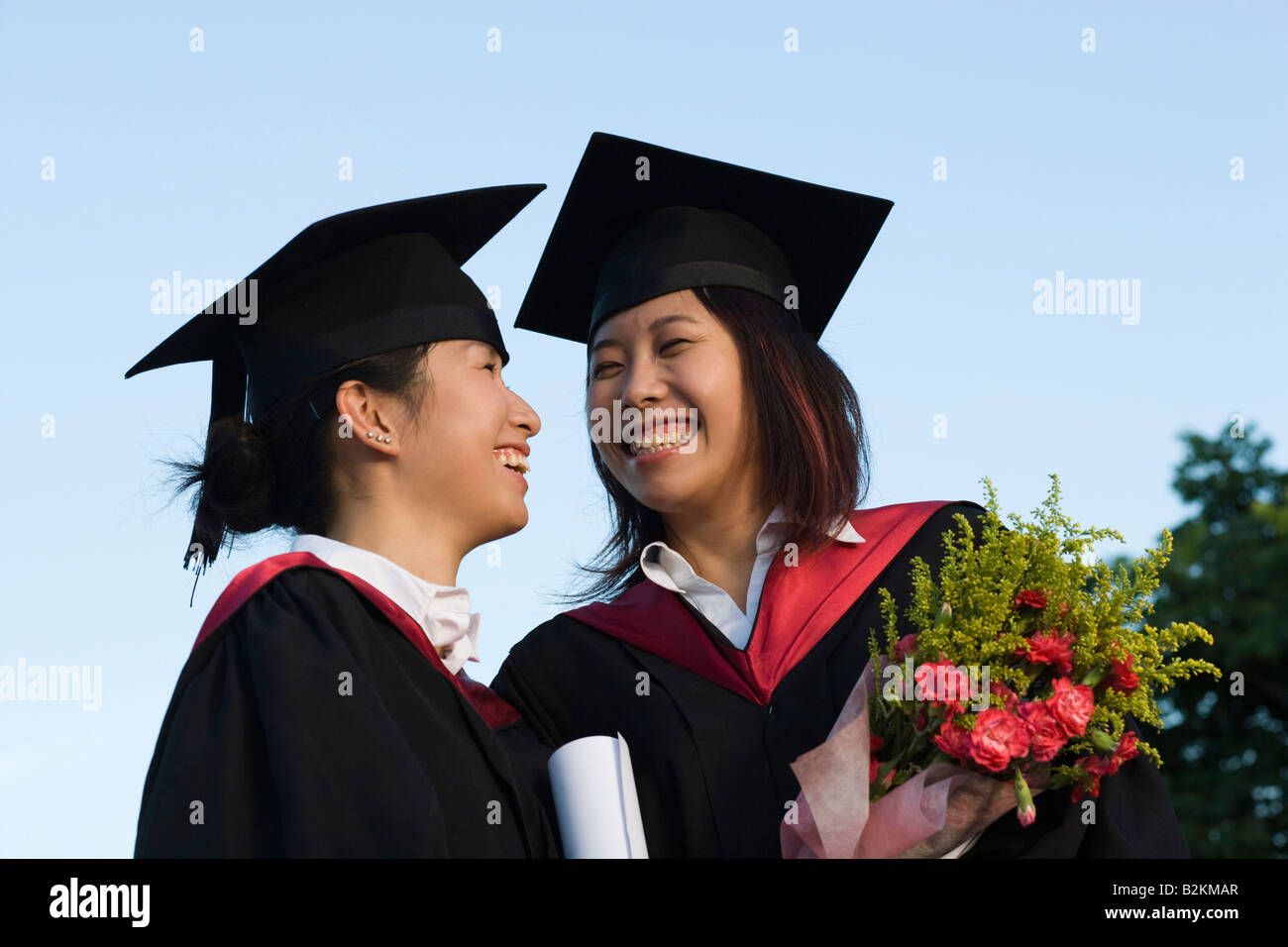 Low angle view of two female graduates holding diplomas and smiling ...