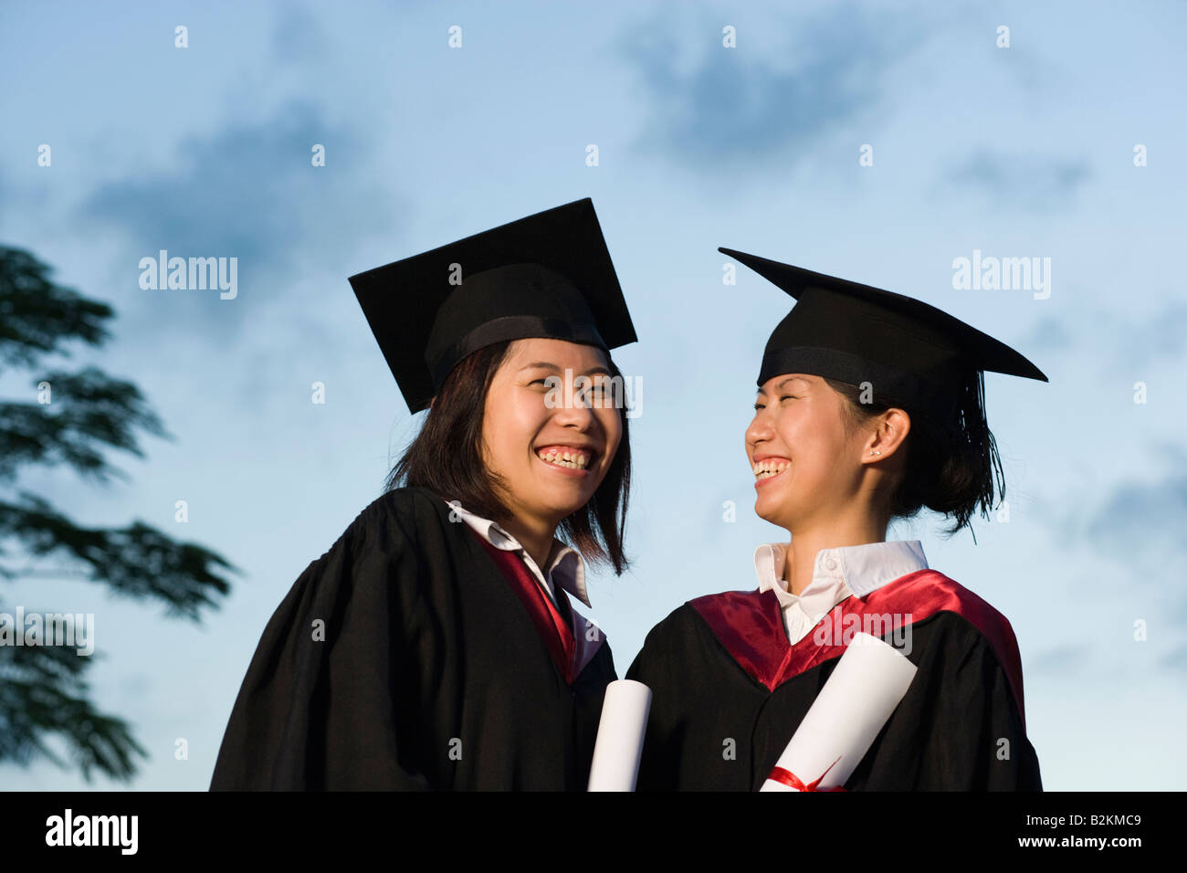 Low angle view of two female graduates holding diplomas and smiling ...