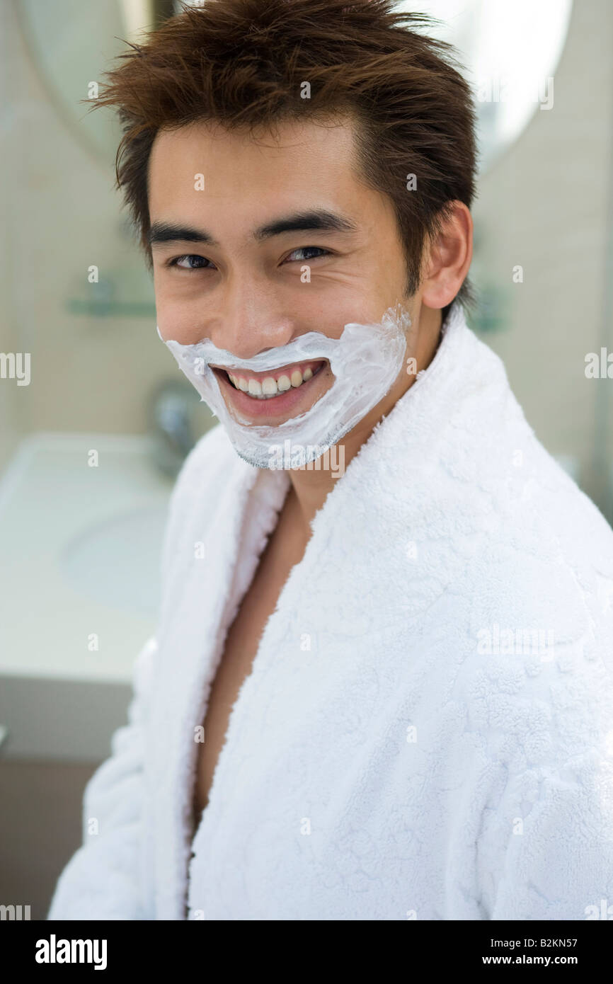 Portrait of a young man applying shaving cream on his face and smiling ...