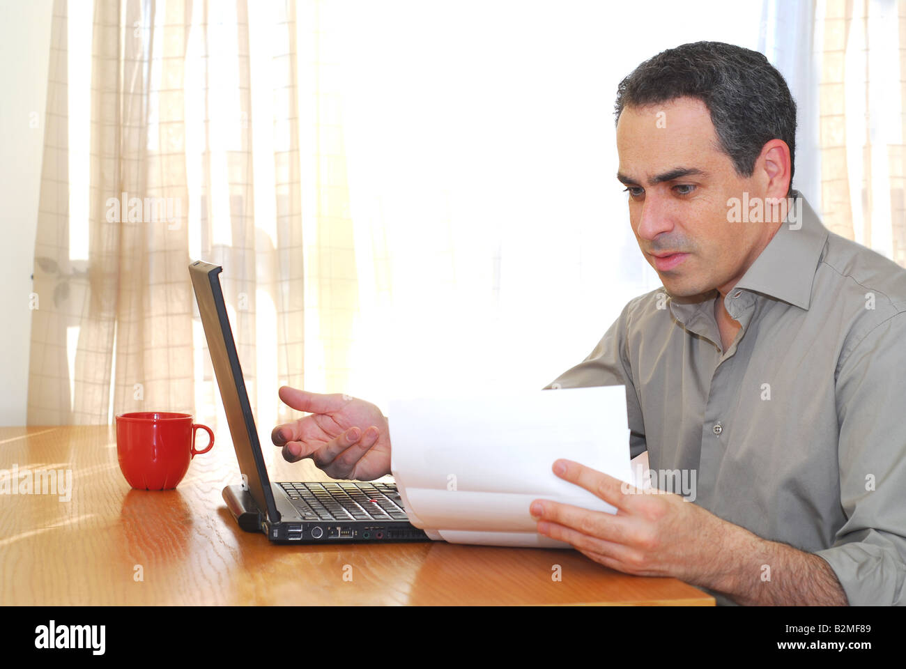 Man sitting at his desk with a laptop looking at bills Stock Photo - Alamy