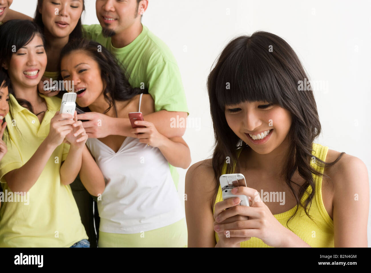 Young woman text messaging with her friends in the background looking ...