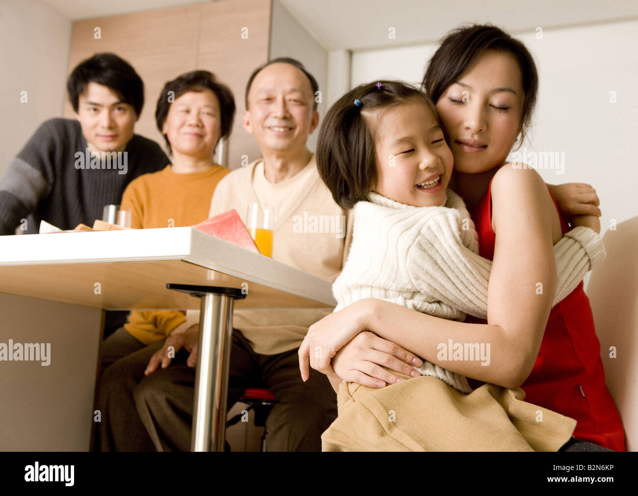 Close-up of a young woman hugging her daughter with her family members ...