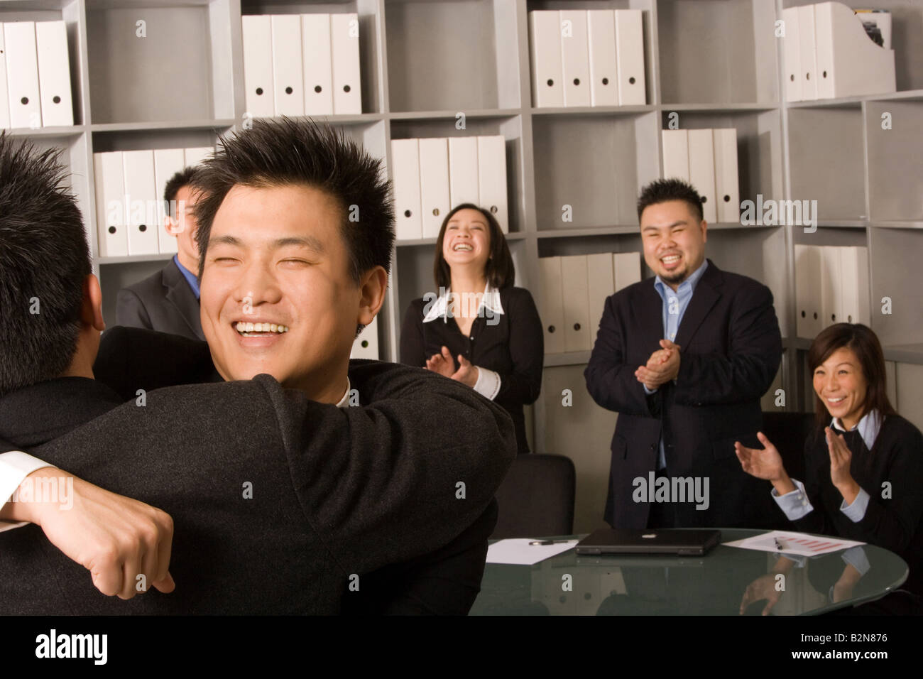 Close-up of two businessmen hugging each other with their colleagues ...