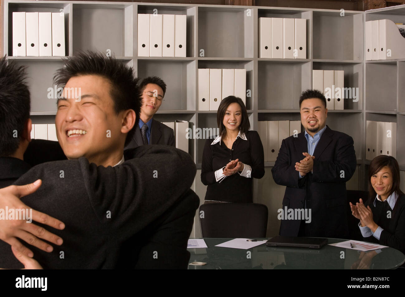 Close-up of two businessmen hugging each other with their colleagues ...