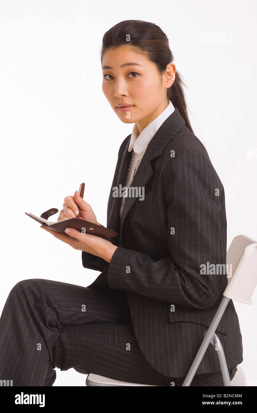 Side profile of a businesswoman sitting on a chair and writing in a ...