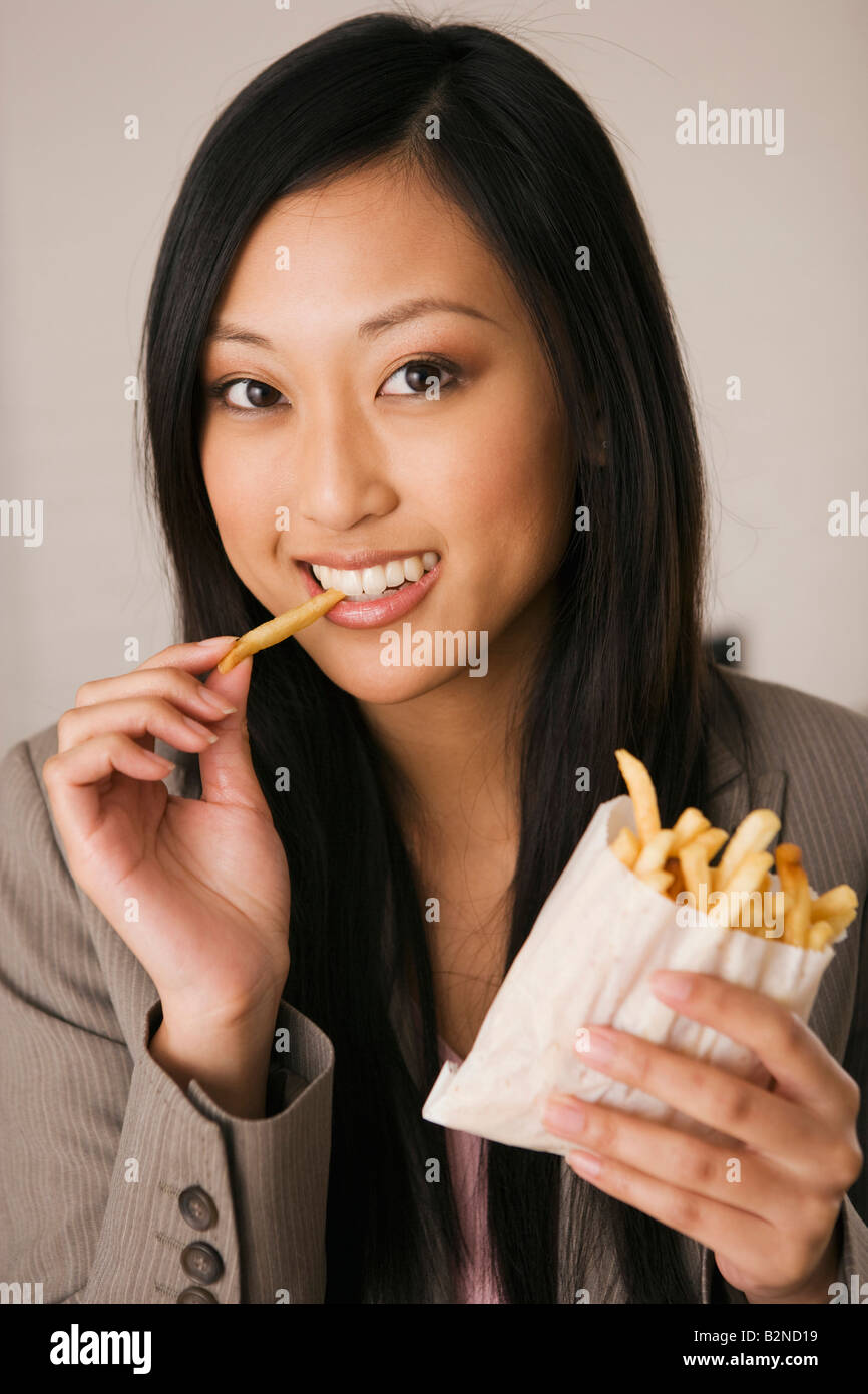 Portrait of a young woman eating French fries and smiling Stock Photo ...