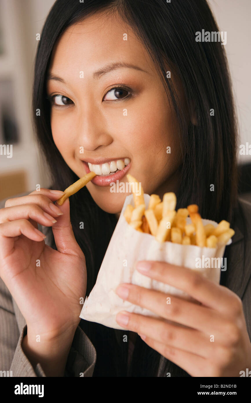 Portrait of a young woman eating French fries and smiling Stock Photo ...