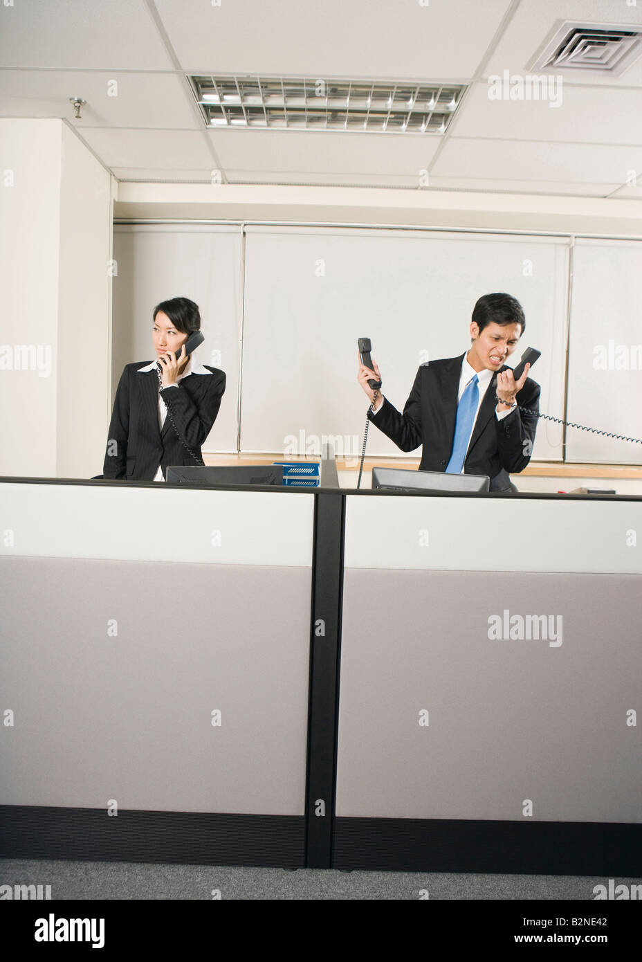 Businessman and a businesswoman talking on landline phones and standing ...