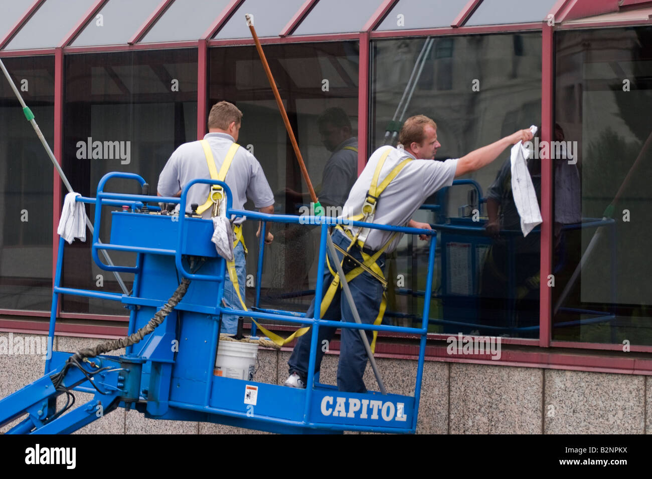 Two men several stories up on a moving platform cleaning the outside ...