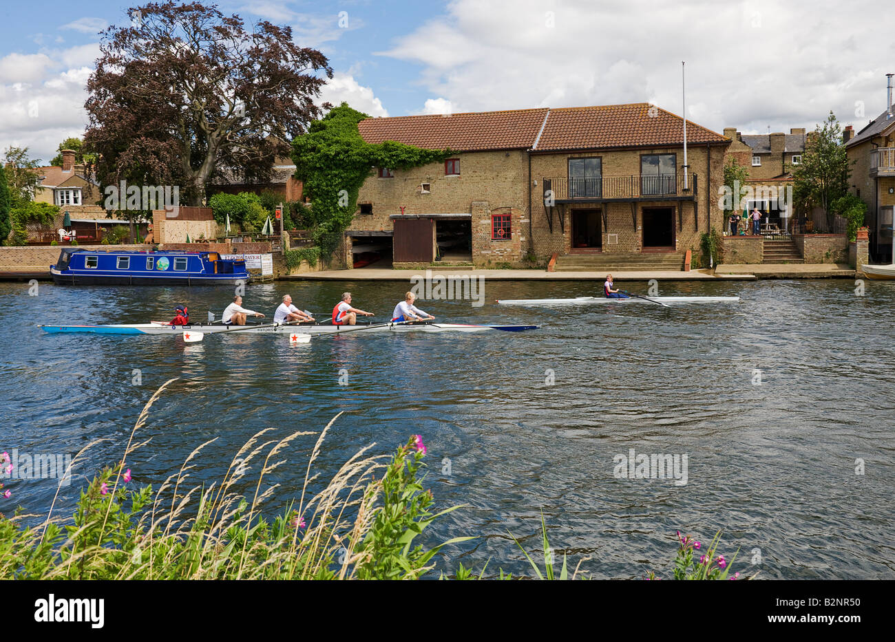 A four seater racing shell passing the rowing club boat house making ...