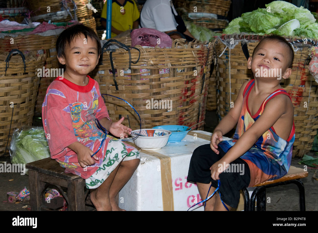 Two happy smiling market children sitting surrounded by baskets of ...