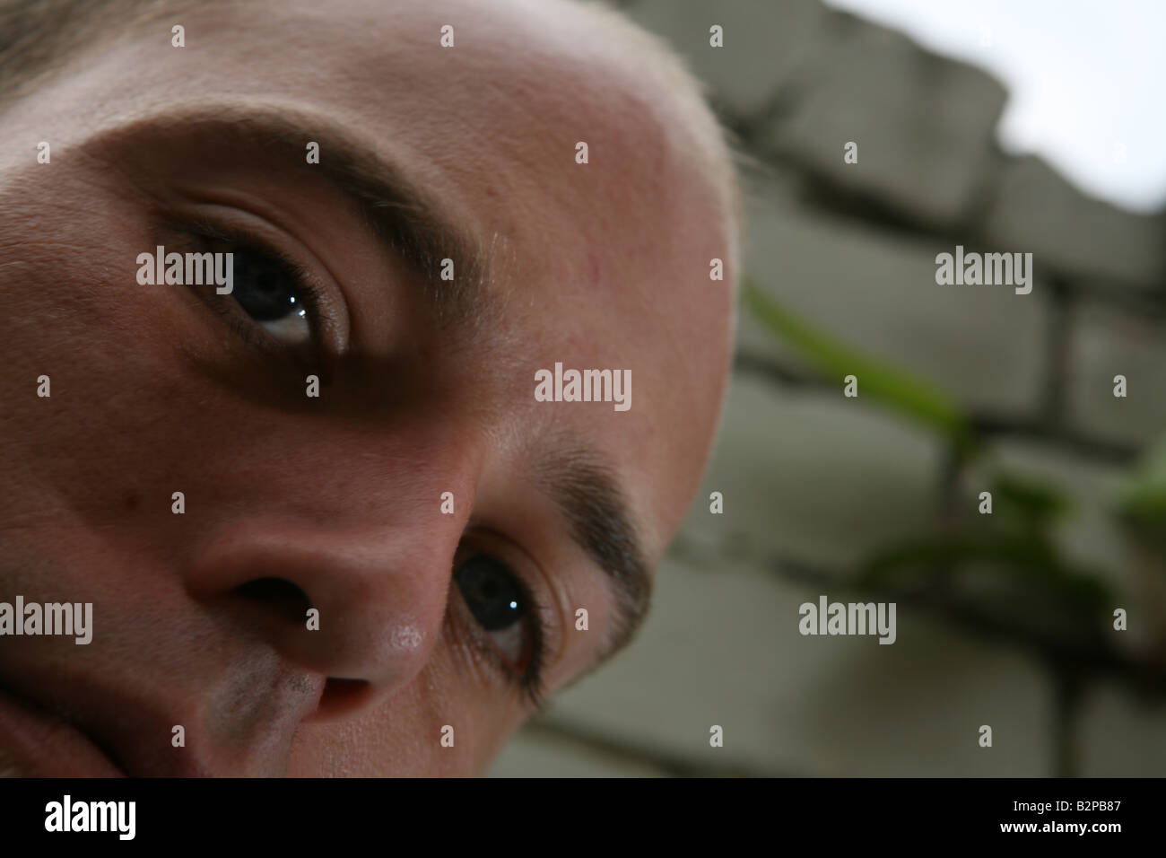 A portrait of a young man looking down into the camera lens with a wall ...