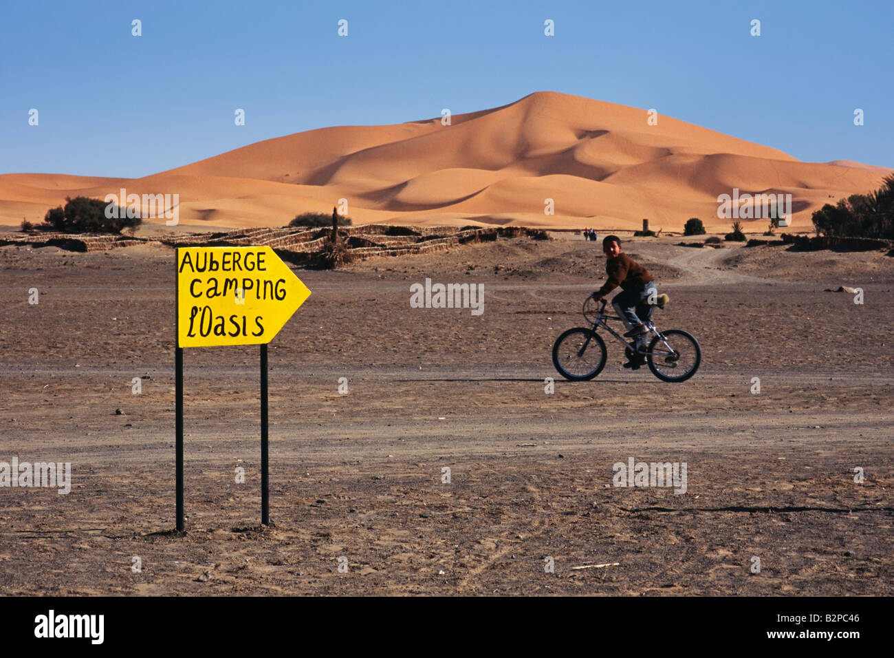 Young boy bicycling past a sign showing the way to a campsite near the ...