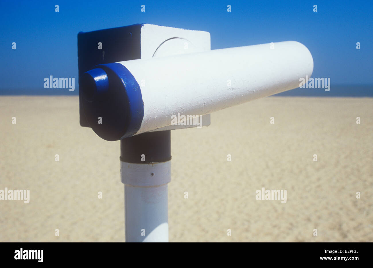 Close up of white and blue seaside telescope with soft pale sand and ...