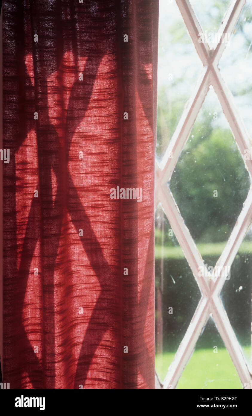 View through period diamond leaded window half hidden by red curtain ...