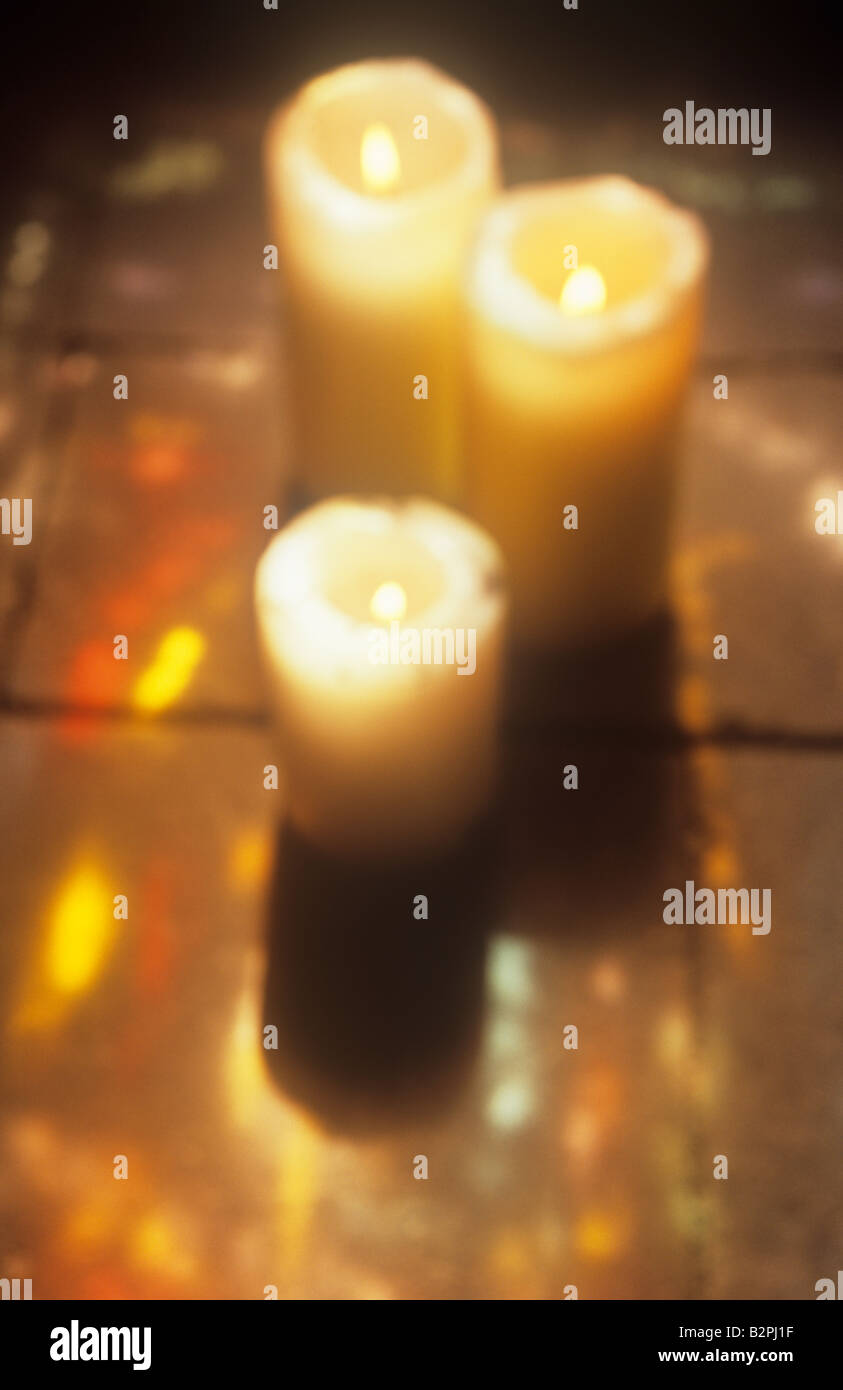 Impressionistic three fat candles flickering in warm light cast by ...