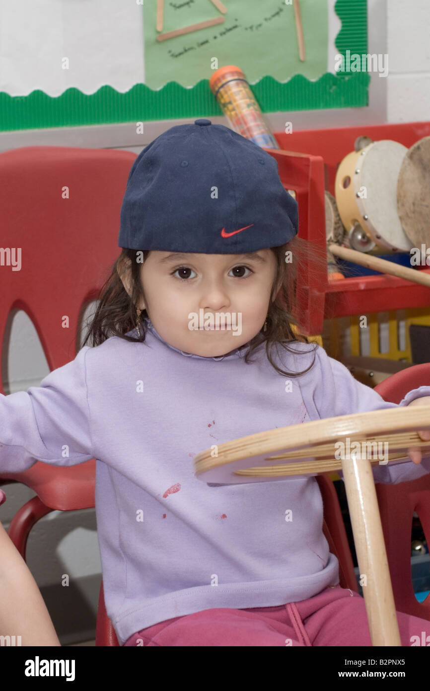 4 year old preschool girl wearing a blue cap backwards looking into the ...