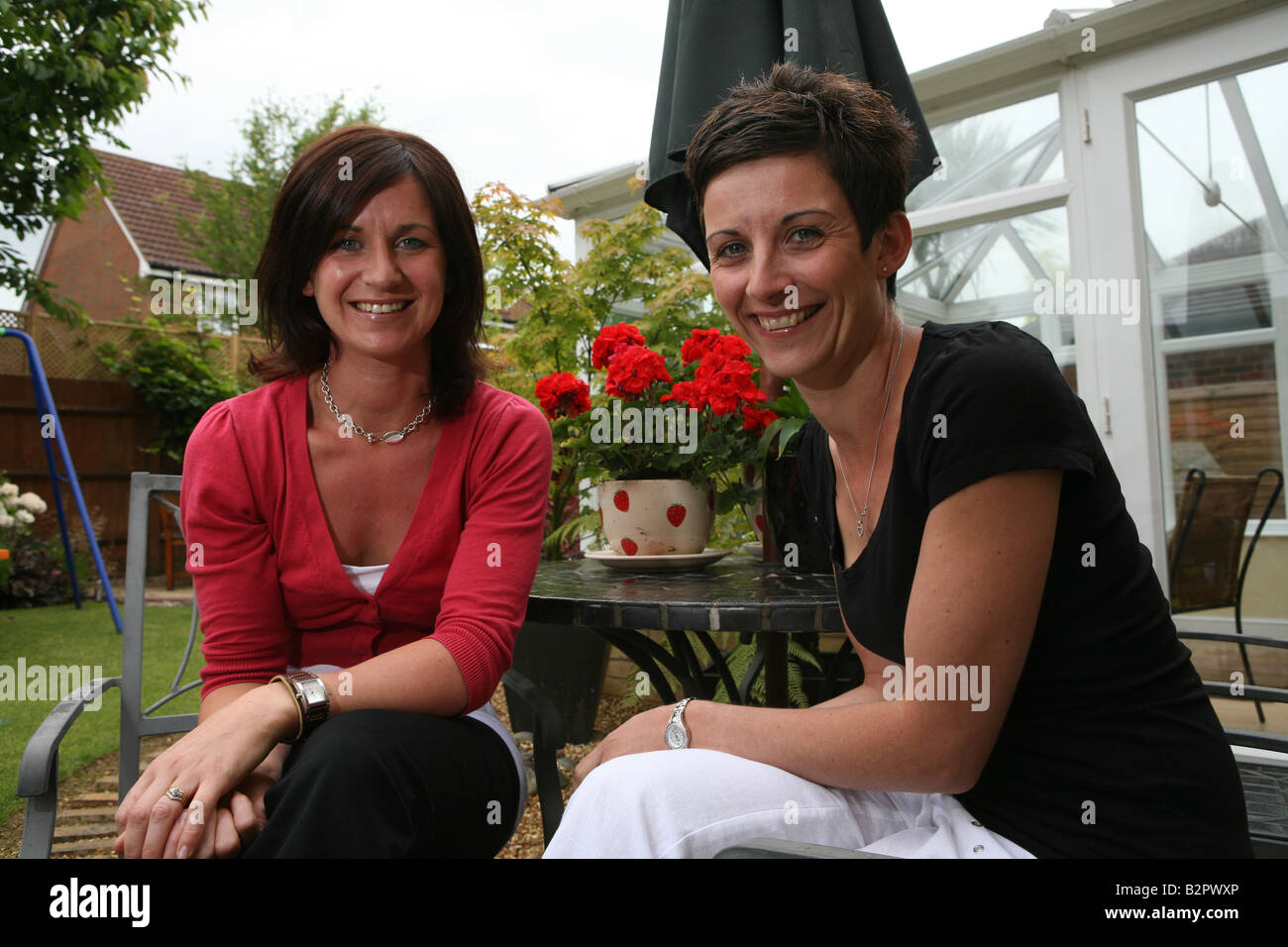 two beautiful sisters sit on some garden funiture in a residential back ...