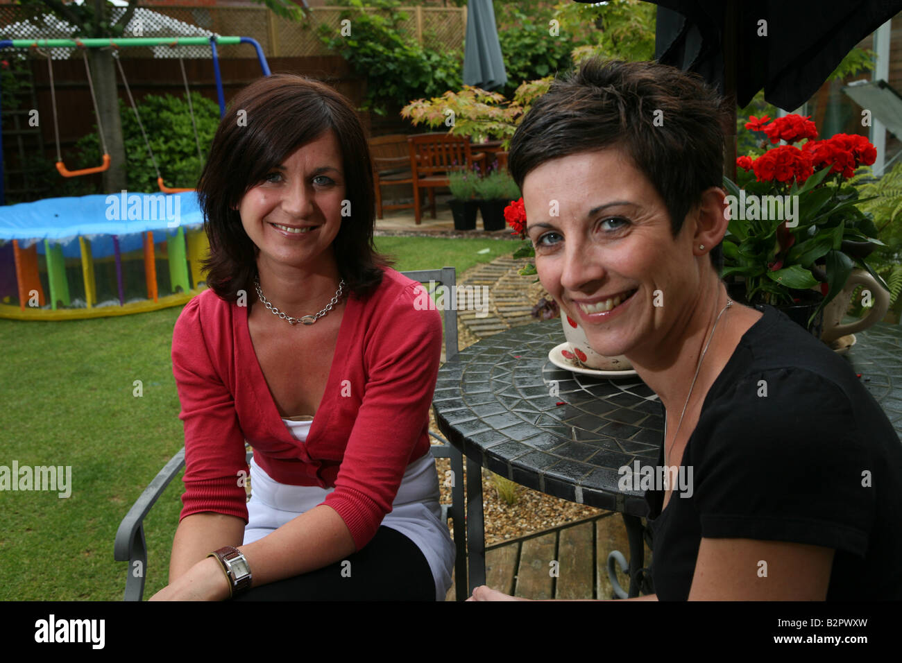 two beautiful sisters sit on some garden funiture in a residential back ...