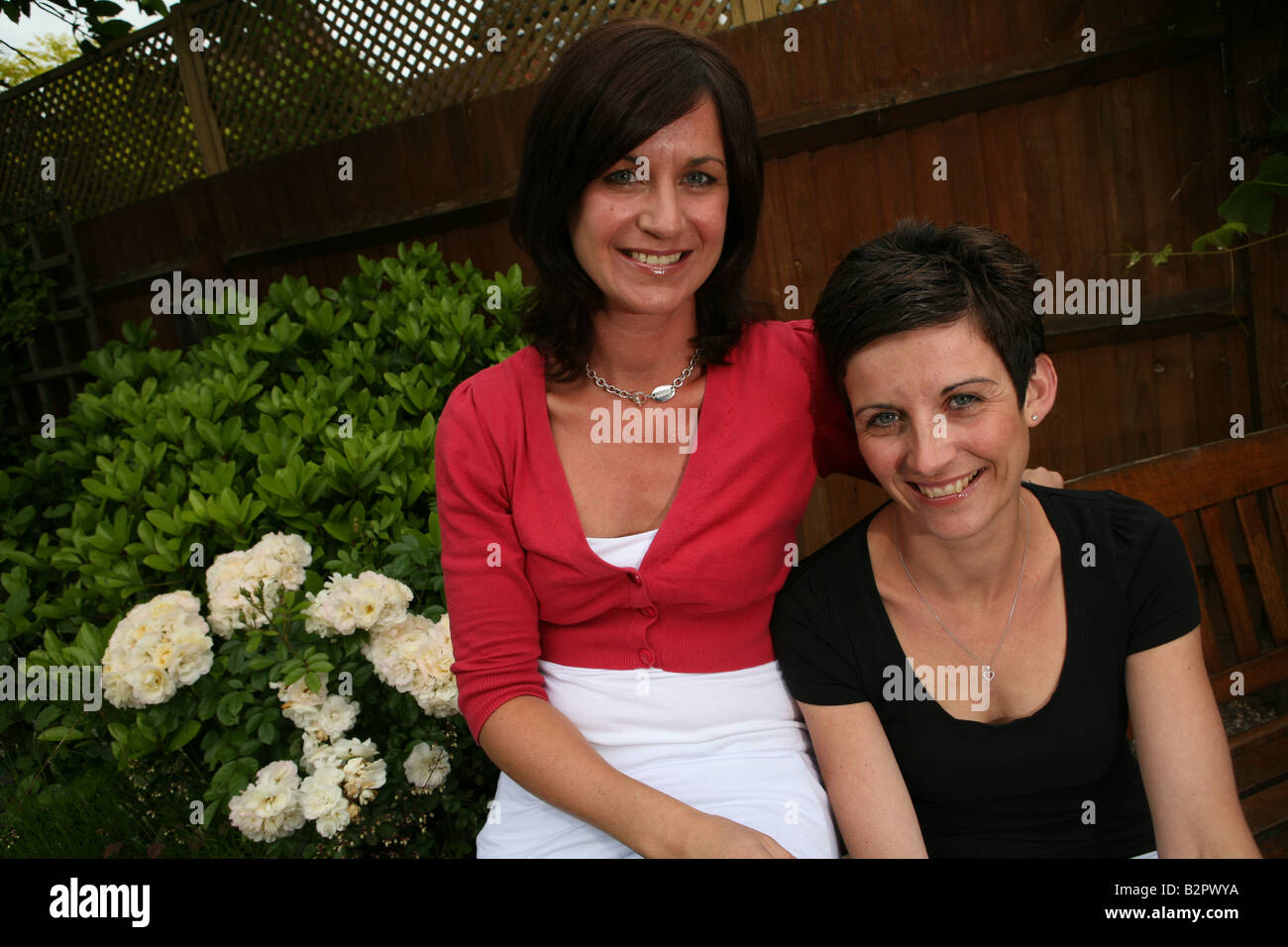 two beautiful sisters sit on some garden funiture in a residential back ...