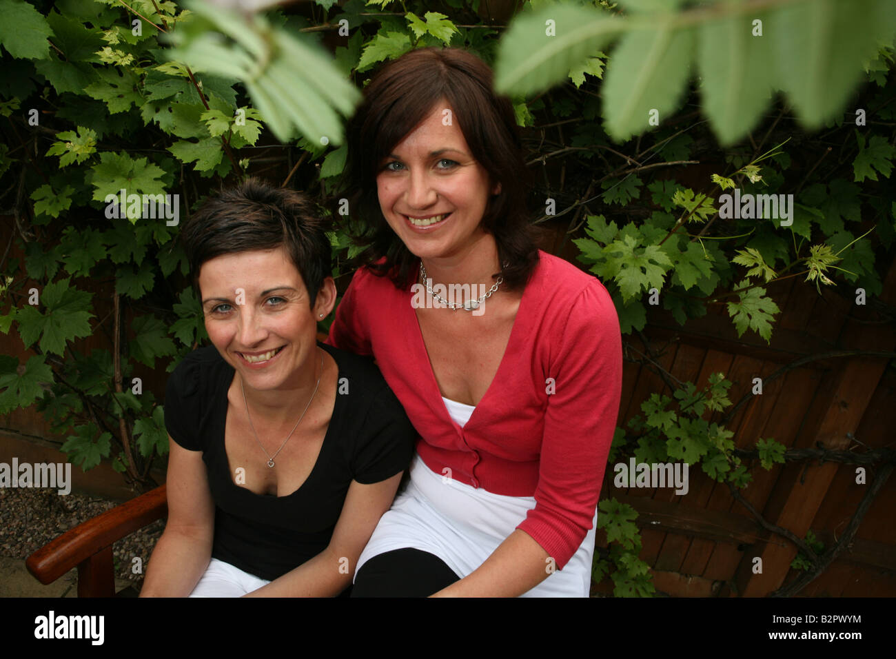 two beautiful sisters sit on some garden funiture in a residential back ...