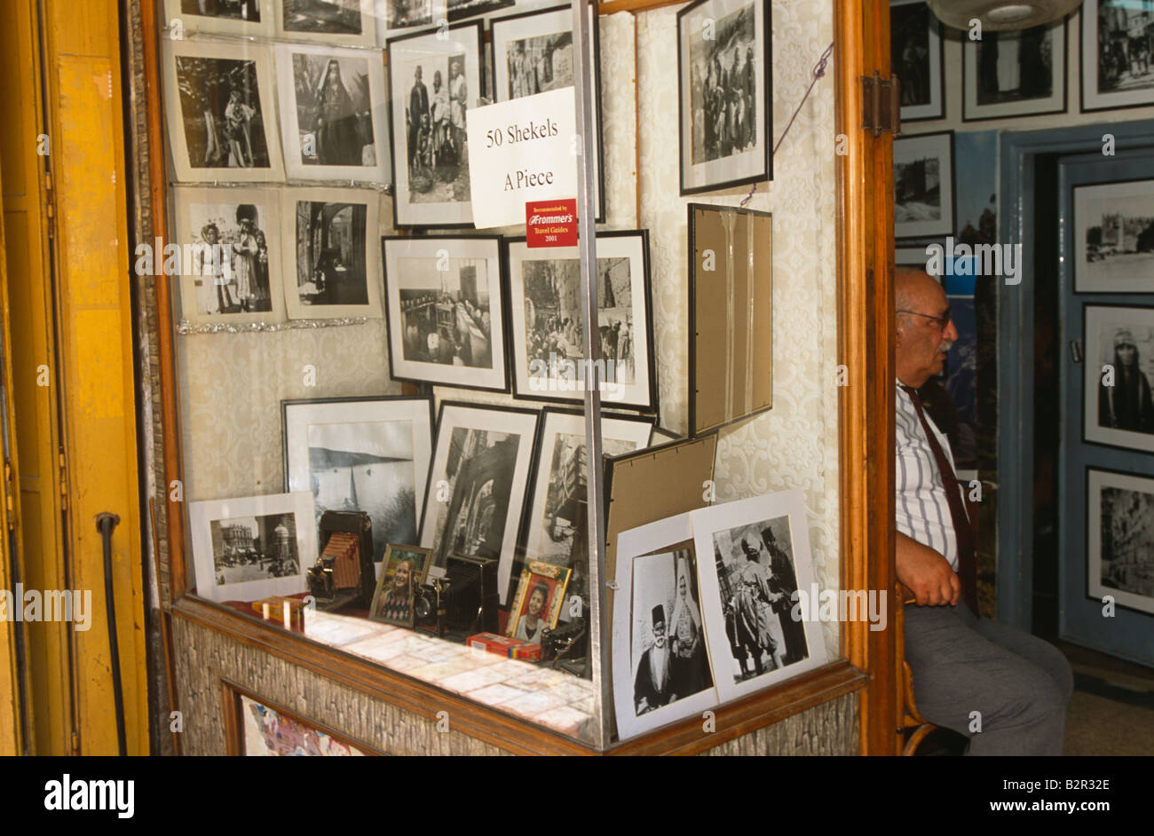 Male shopkeeper sitting inside shop displaying old photographs in shop ...