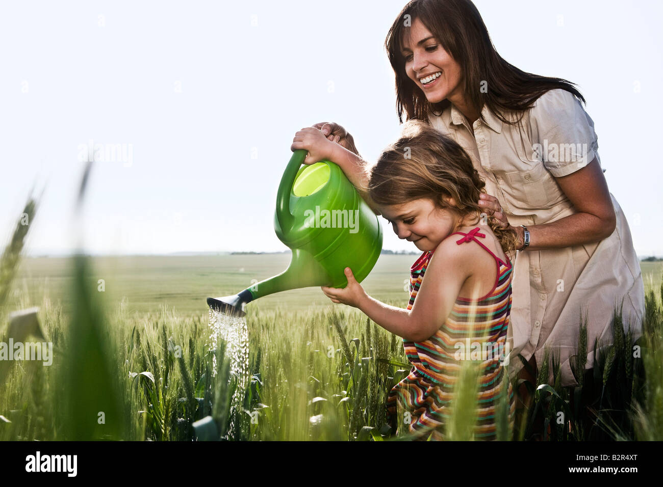 Woman helping child with watering can Stock Photo - Alamy