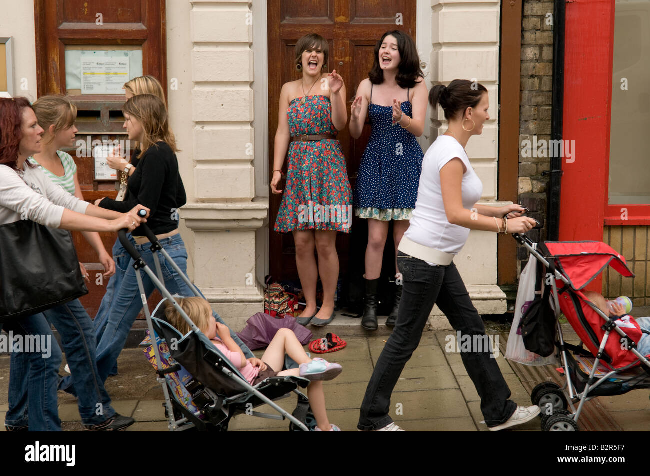 two young teenage girls singing busking on the street as women walk by ...