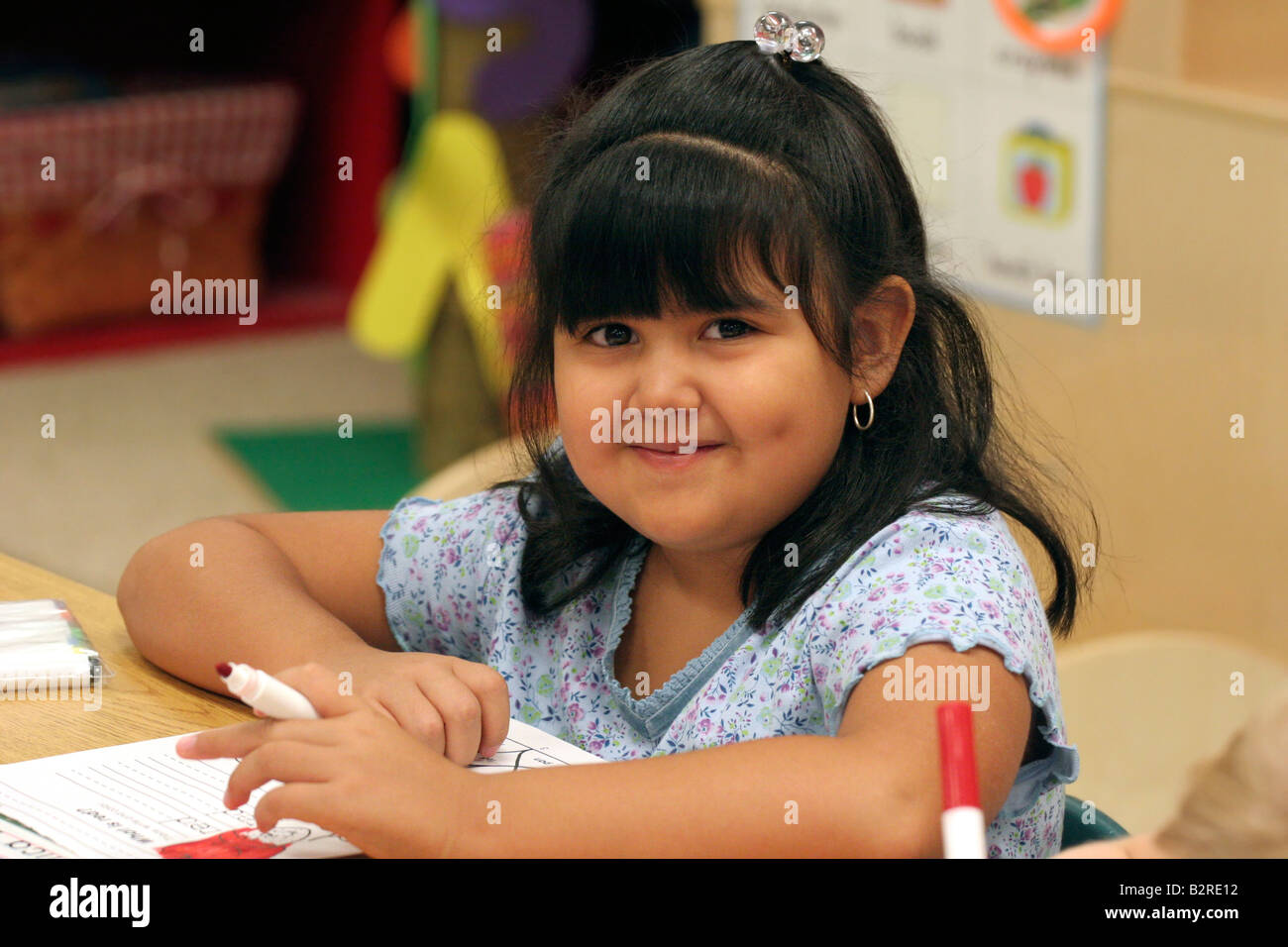 Young Hispanic Kindergarten girl uses marker to work on activity sheet ...